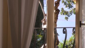 Uma janela com cortinas brancas, vista para folhas de outono e um corrimão de metal.