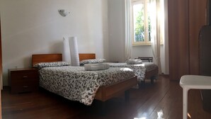 Quarto com duas camas, uma mesinha de cabeceira de madeira, uma cadeira branca e um guarda-roupa.