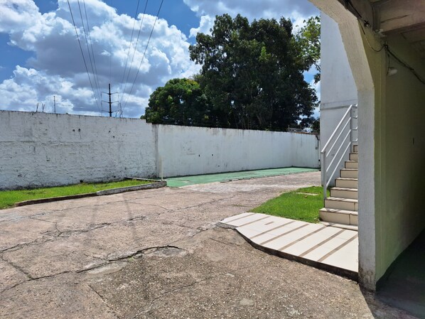 Um pátio com uma parede branca, um tapete verde e uma escadaria que leva a um andar superior.