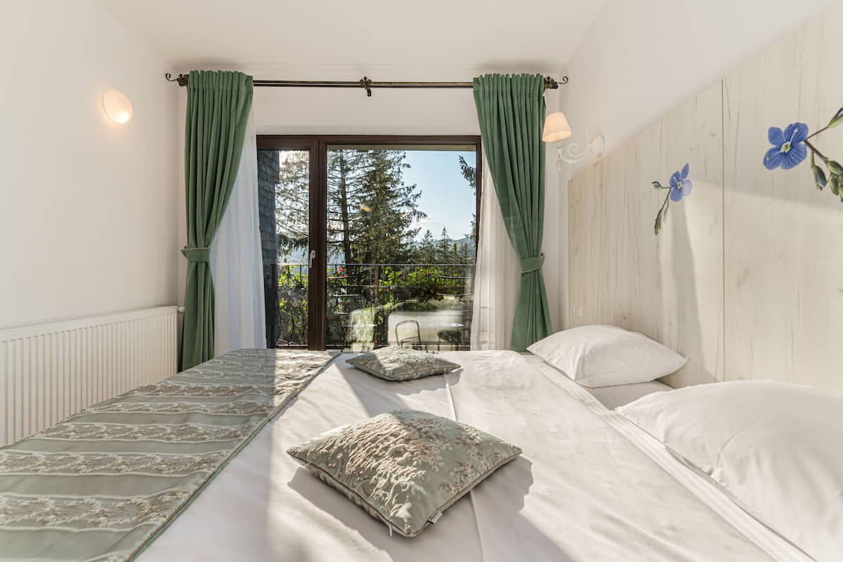 Quarto com cama, almofadas e vista para uma varanda.