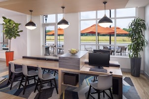 Um escritório moderno com uma mesa comprida, várias cadeiras, um computador e vista para um campo através de grandes janelas.