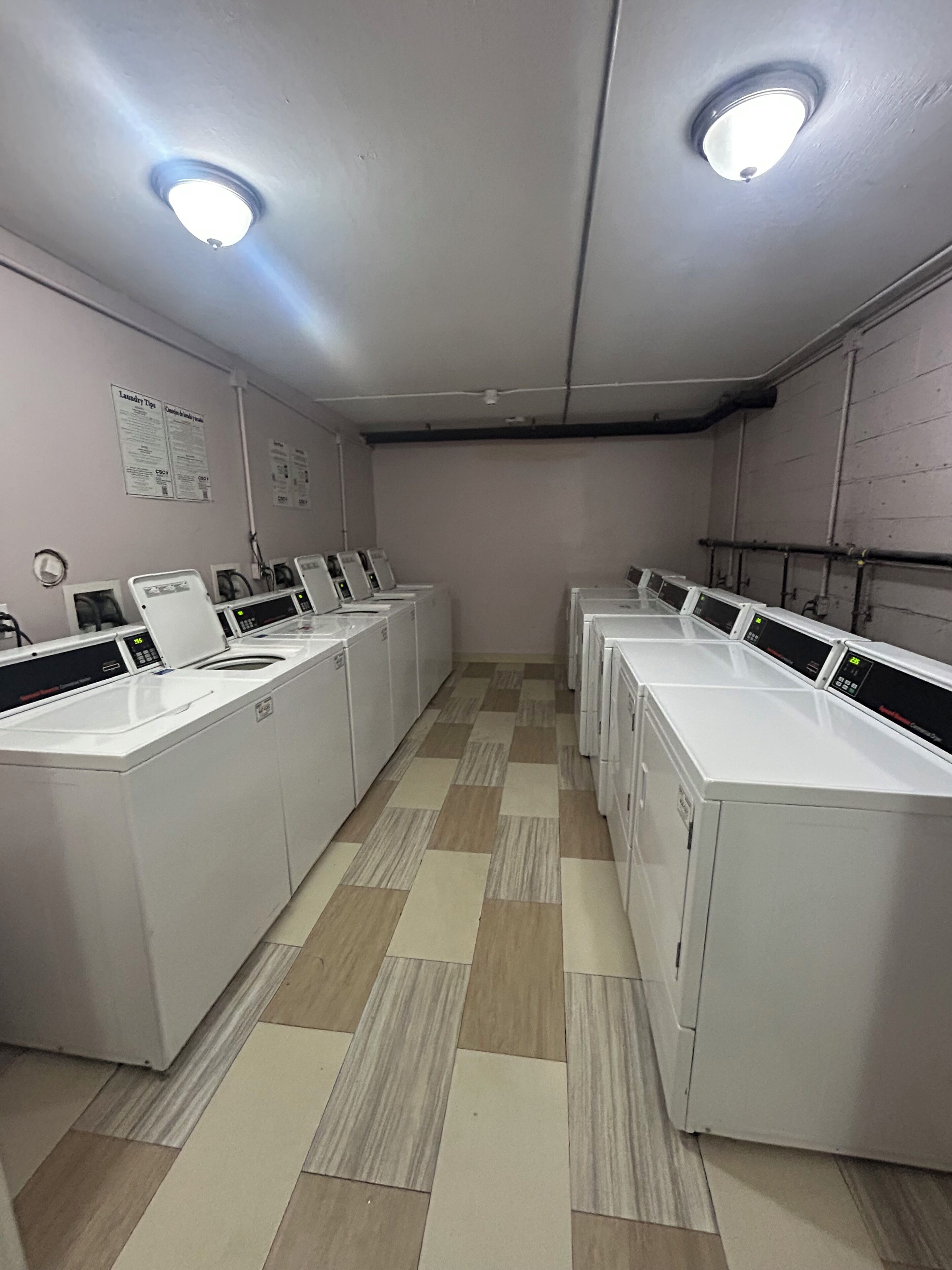 Uma lavanderia com várias máquinas de lavar, piso revestido com azulejos e iluminação no teto.