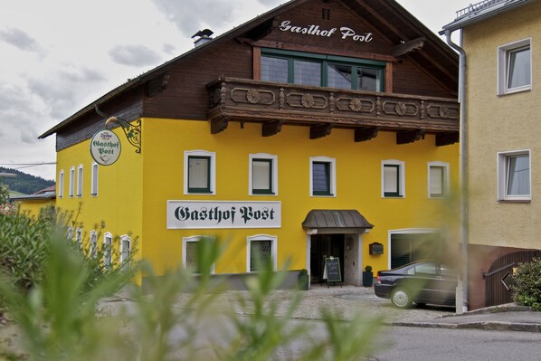 Um edifício amarelo com uma placa indicando "Gasthof Post" e uma varanda com guarda-corpo de madeira.