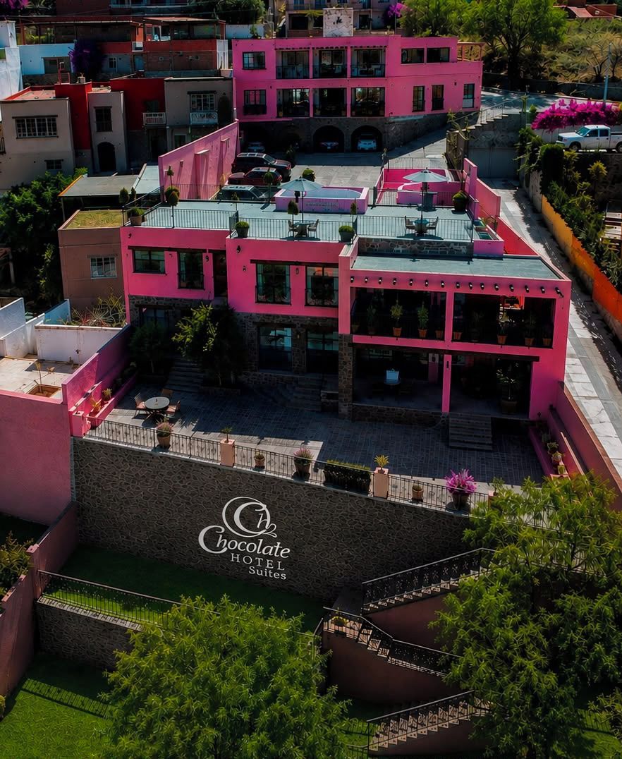 Um hotel com fachada rosa marcante, várias varandas e uma placa indicando ser o Chocolate Hotel Suites.