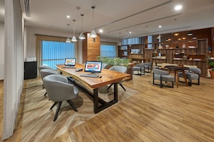 Uma sala de conferências moderna com mesa de madeira, cadeiras cinzas e uma janela grande com cortinas.