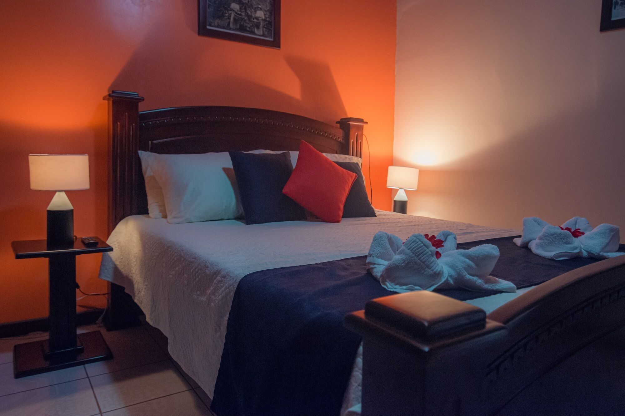 Cama bem arrumada com almofadas, mesa de cabeceira com abajur e toalhas sobre a cama.