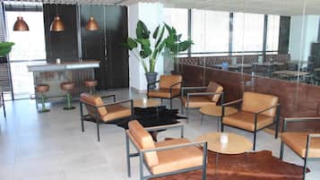 Uma área de estar moderna com sofás de couro, mesas redondas e um balcão de bar.