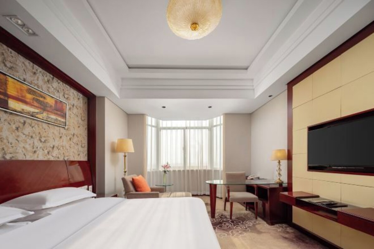 Quarto de hotel com uma cama grande, uma mesa, uma televisão e uma janela com cortinas.