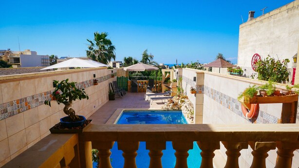 Uma área de piscina no terraço com vista para o mar, rodeada por plantas em vasos e mobiliário de exterior.