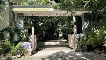 Uma passagem que leva a um portão com pérgola, cercada por vegetação exuberante e uma parede de pedra.