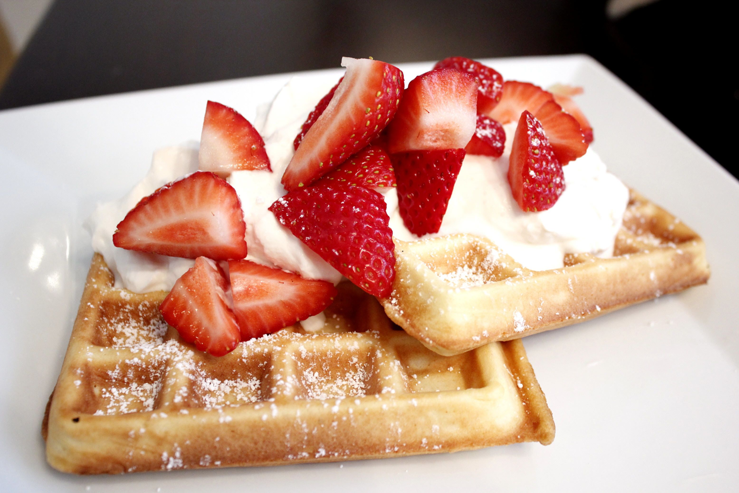 Waffle coberto com chantilly e morangos fatiados.