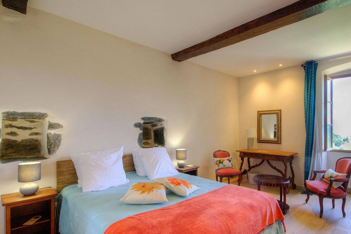 Quarto com cama, mesas de cabeceira, escrivaninha e cadeiras.