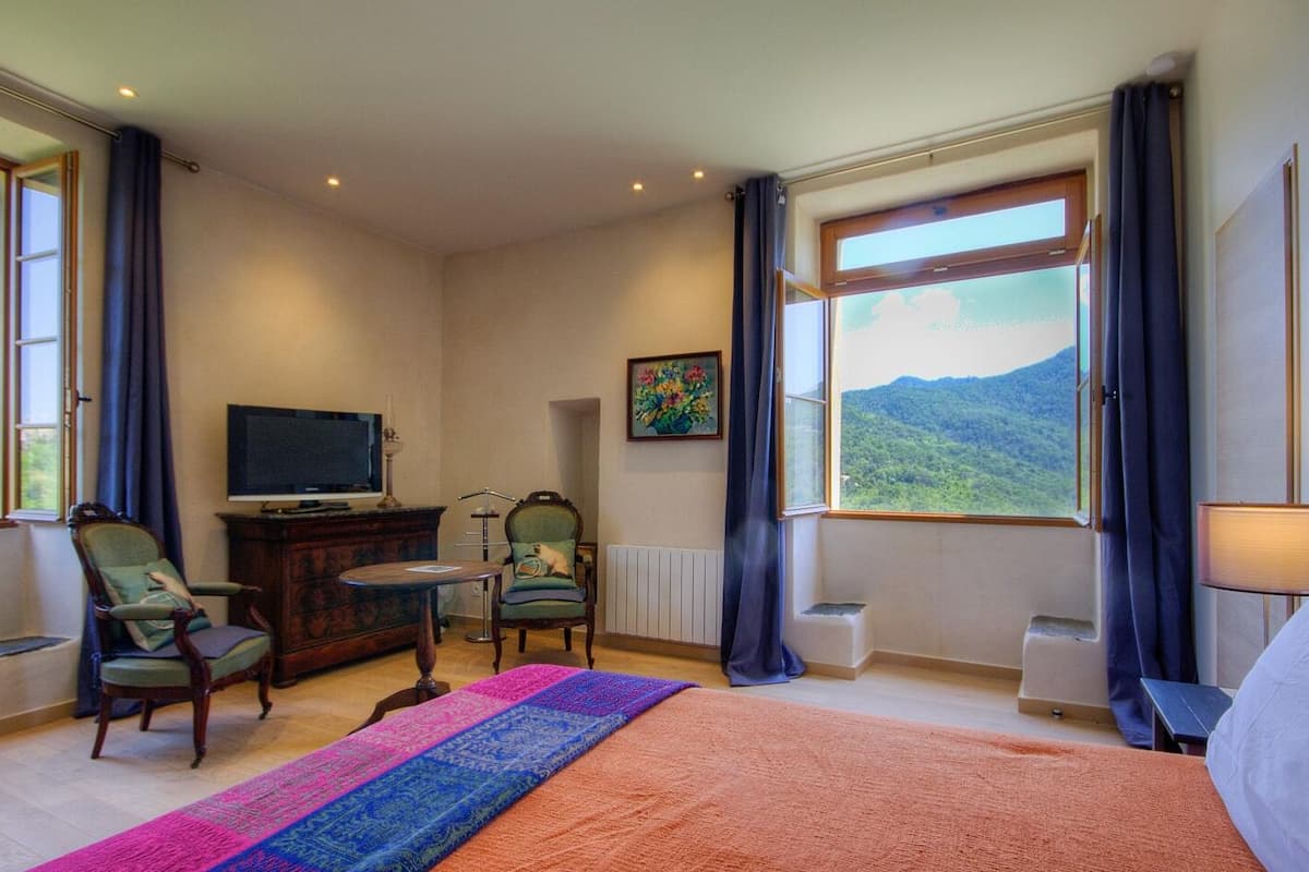 Quarto de hotel com cama, escrivaninha, cadeira, televisão e vista para as montanhas.