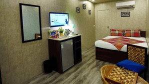 Quarto de hotel com uma cama, uma escrivaninha com um computador, um mini-refrigerador e uma televisão exibindo uma mensagem.