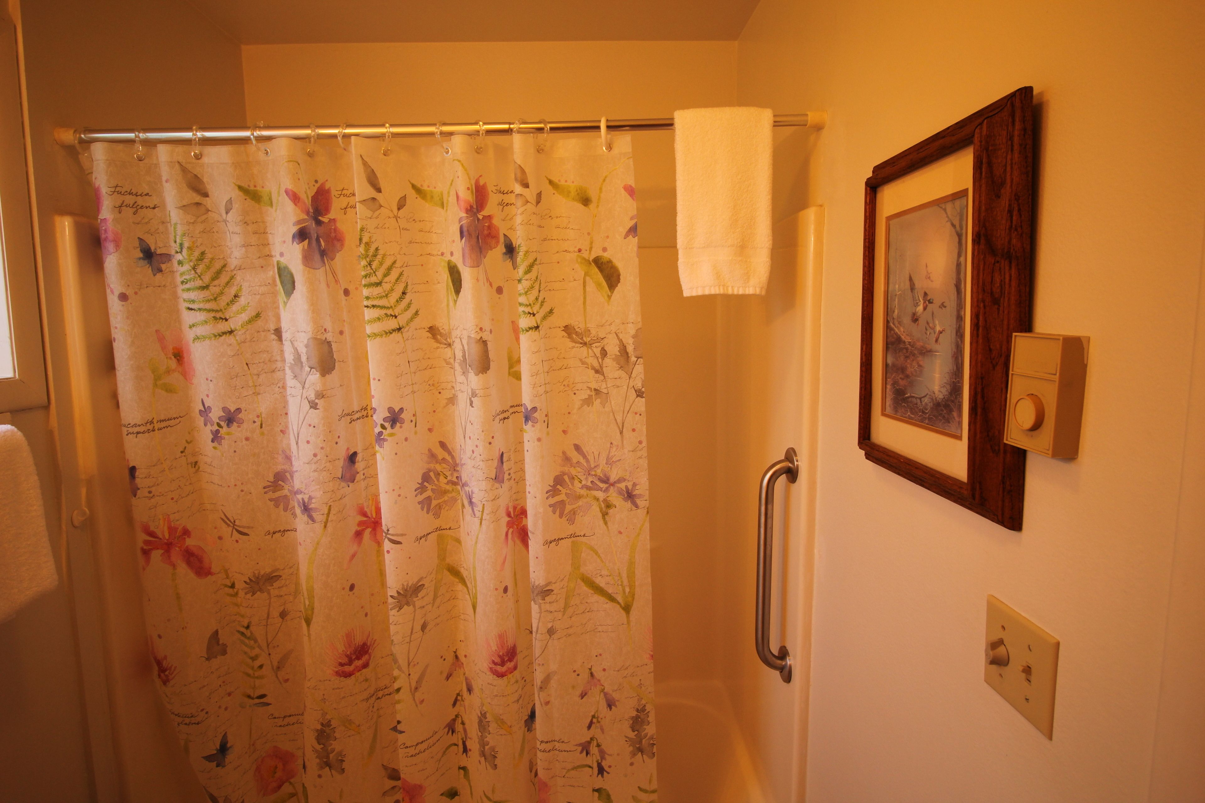 Um banheiro com cortina de chuveiro estampada com flores, um corrimão, um quadro na parede e uma toalha pendurada na porta.