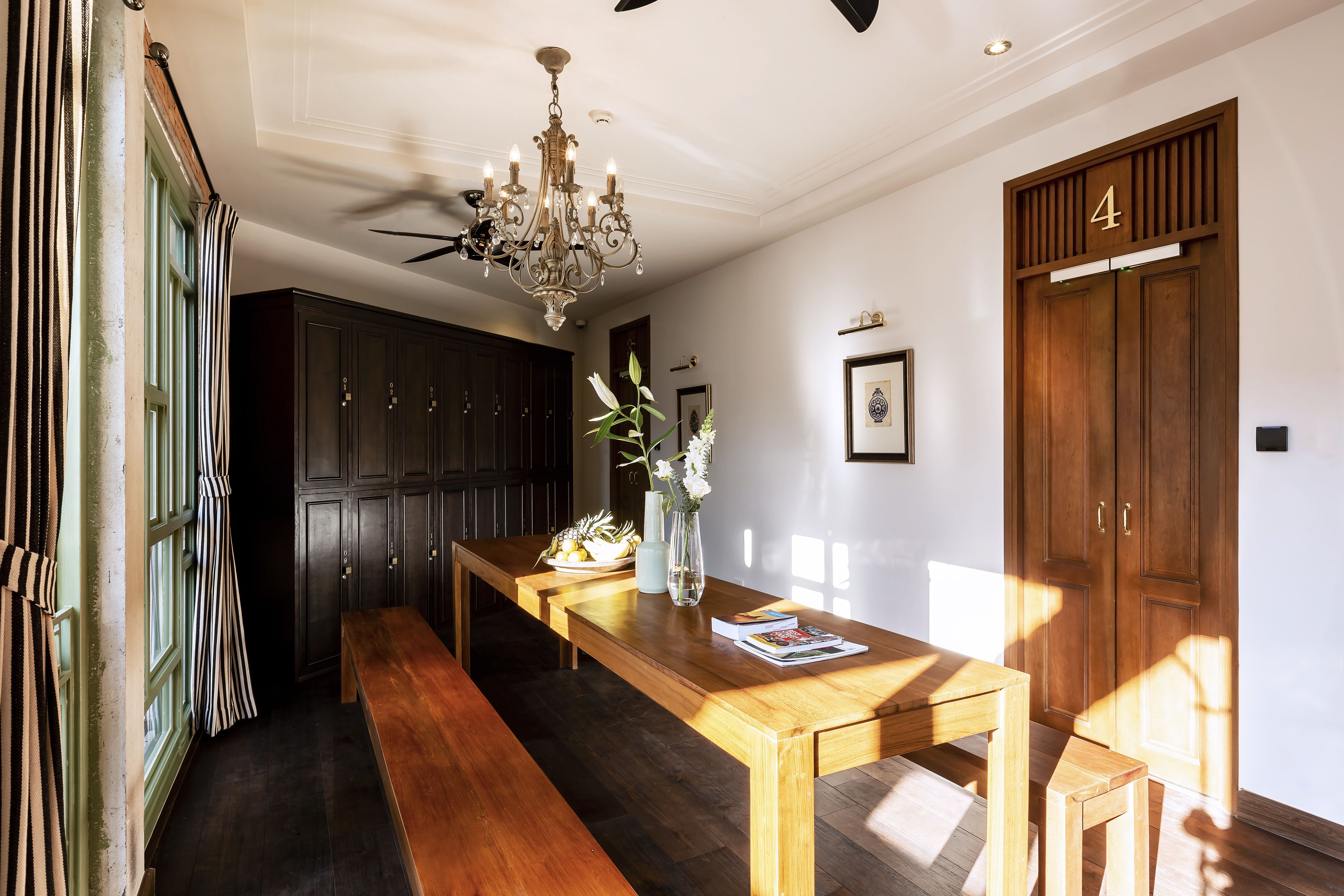 Um corredor espaçoso com um banco de madeira, uma mesa de jantar com um vaso de flores e um candelabro.