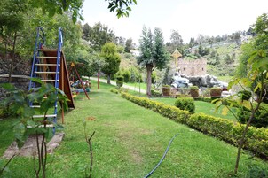 Um jardim bem cuidado com área de recreação infantil, sebes podadas e uma estrutura de pedra que lembra um castelo.
