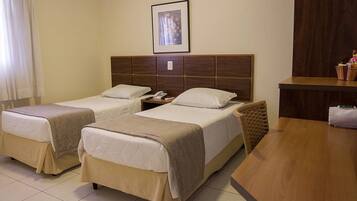 Quarto de hotel com duas camas, cabeceira de madeira, mesa de cabeceira com abajur e um quadro pendurado na parede.