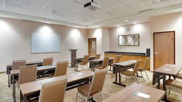 Uma sala de conferências com várias mesas e cadeiras, um projetor, um relógio e uma porta de madeira.