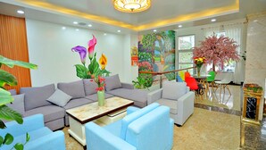 Uma sala de estar moderna com um sofá seccional, uma mesa de centro e um lustre. Há cadeiras coloridas e uma área de refeições ao fundo.