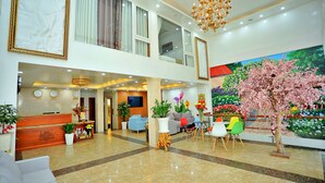 Um sagu ão de hotel com uma mesa de recepção, área de estar e uma grande pintura de uma cerejeira.