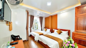 Quarto de hotel com duas camas, uma escrivaninha com cadeira, televisão, ventoinha e janela com cortinas.