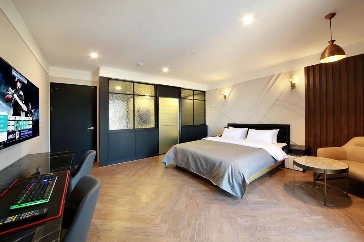 Quarto de hotel moderno com uma cama, uma escrivaninha com computador, uma cadeira e uma televisão.