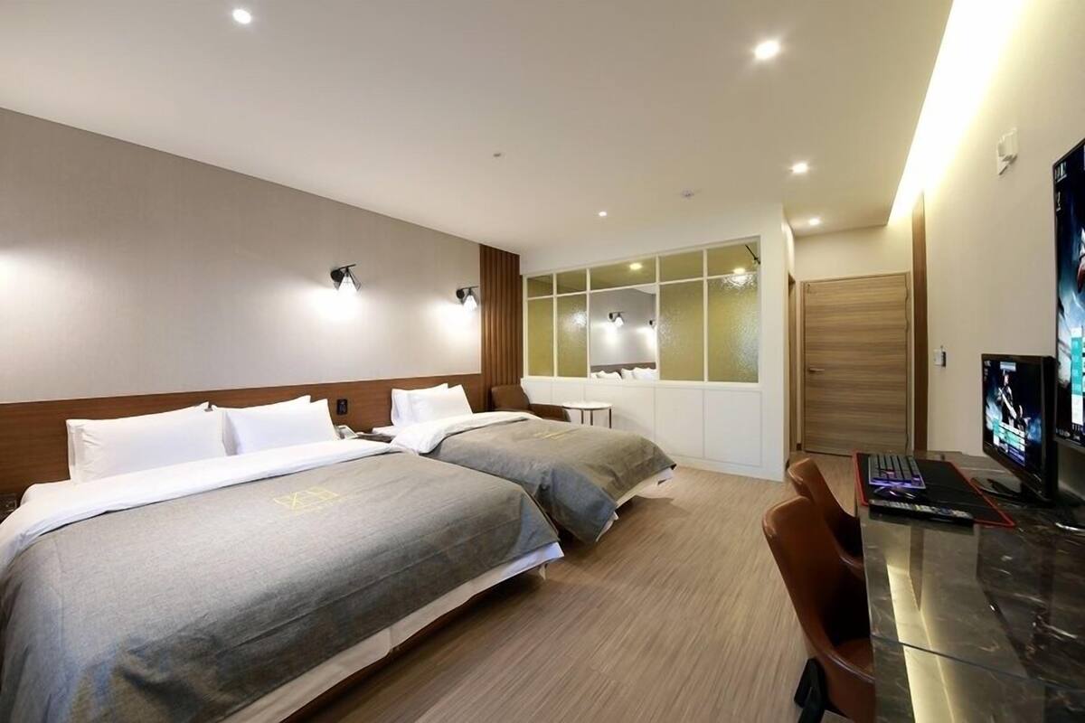 Quarto de hotel com duas camas, uma escrivaninha com computador e uma televisão.