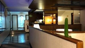 Um hall de hotel moderno com um balcão de recepção curvo, uma grande decoração de cacto e vista para o espaço interno.