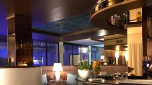 Uma área de bar moderna com balcão curvo, assentos iluminados por luminárias e vista para o salão.