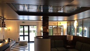 Um saguão com piso xadrez, um pilar central, área de estar e balcão de recepção.