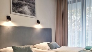 Quarto de hotel com duas camas, cada uma com cabeceira, um quadro na parede e uma janela com cortinas.