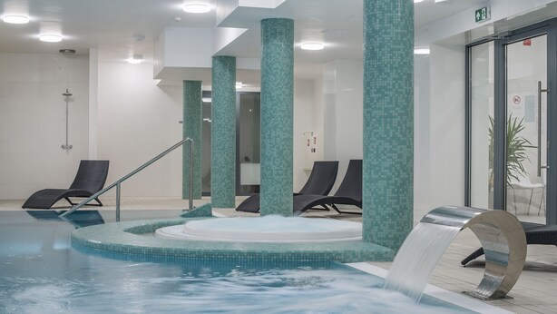 Piscina interna moderna com hidromassagem, espreguiçadeiras e um elemento aquático.