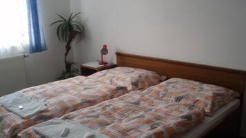 Uma cama de casal com roupa de cama estampada, uma mesa de cabeceira com abajur e um vaso de planta.