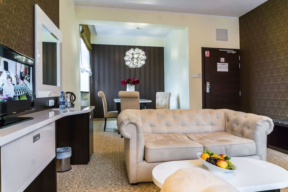 Quarto de hotel com sofá, mesa de jantar e cadeiras, televisão e uma fruteira.