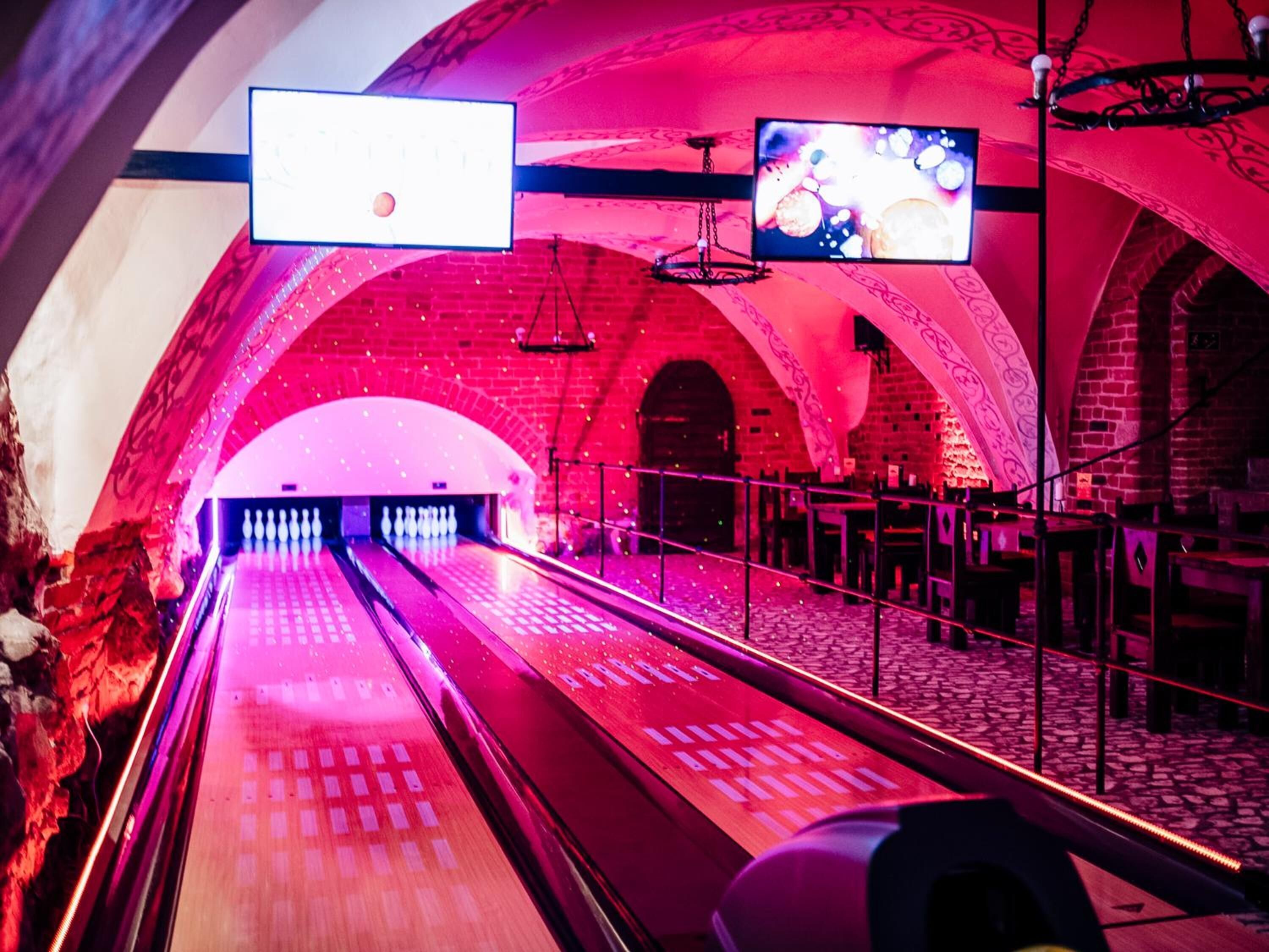 Boliche com ambiente iluminado em néon vermelho, várias pistas e parede de tijolos.