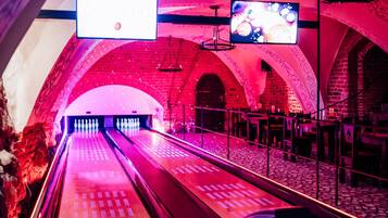 Boliche com ambiente iluminado em néon vermelho, várias pistas e parede de tijolos.