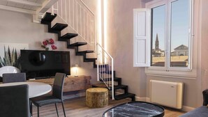 Uma sala de estar moderna com escada, área de refeições e vista para um edifício pela janela.