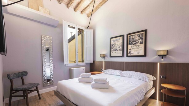 Quarto de hotel moderno com uma cama grande, uma cadeira, um espelho e obras de arte na parede.