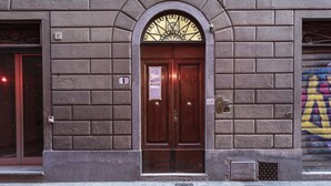 Fachada de edifício com porta dupla de madeira, arco de metal acima da porta e parede de tijolos.