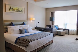 Quarto de hotel com uma cama grande, uma escrivaninha, uma cadeira e vista da cidade pela janela.