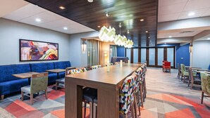 Uma sala de conferências moderna com uma mesa comprida, sofás azuis e cadeiras estampadas.