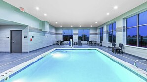 Piscina interior moderna com água cristalina, rodeada por espreguiçadeiras e uma parede de vidro.