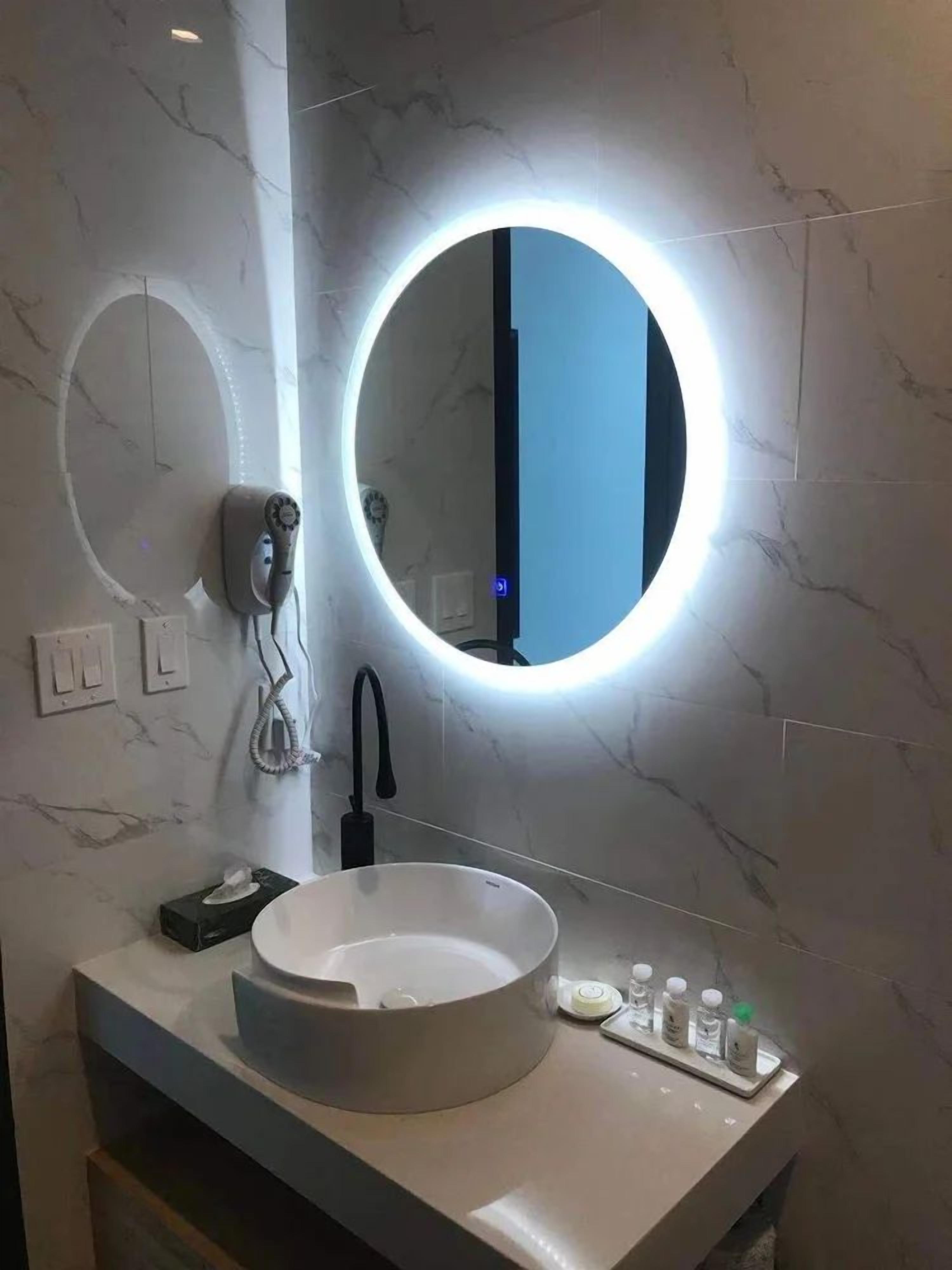 Casa de banho com espelho redondo, secador de cabelo e lavatório com artigos de higiene.