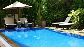 Piscina retangular com borda ladrilhada, rodeada por espreguiçadeiras e um grande guarda-sol.