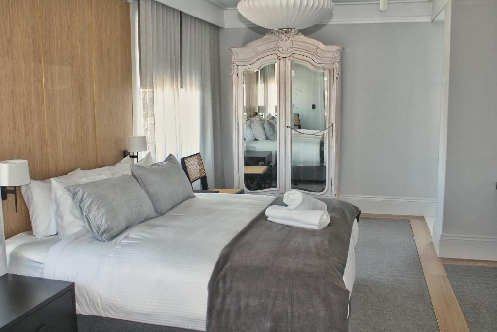 Quarto de hotel com uma cama grande, um guarda-roupa, um espelho e uma mesa de cabeceira.