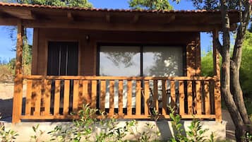Uma cabana de madeira com varanda, janelas amplas e vista para o verde ao redor.
