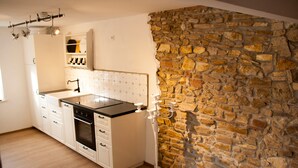 Cozinha com armários brancos, bancada preta, forno embutido e parede de pedra.