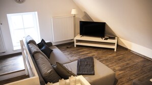Uma sala de estar moderna com um sofá seccional, uma TV de tela plana em um suporte, uma luminária e um radiador.