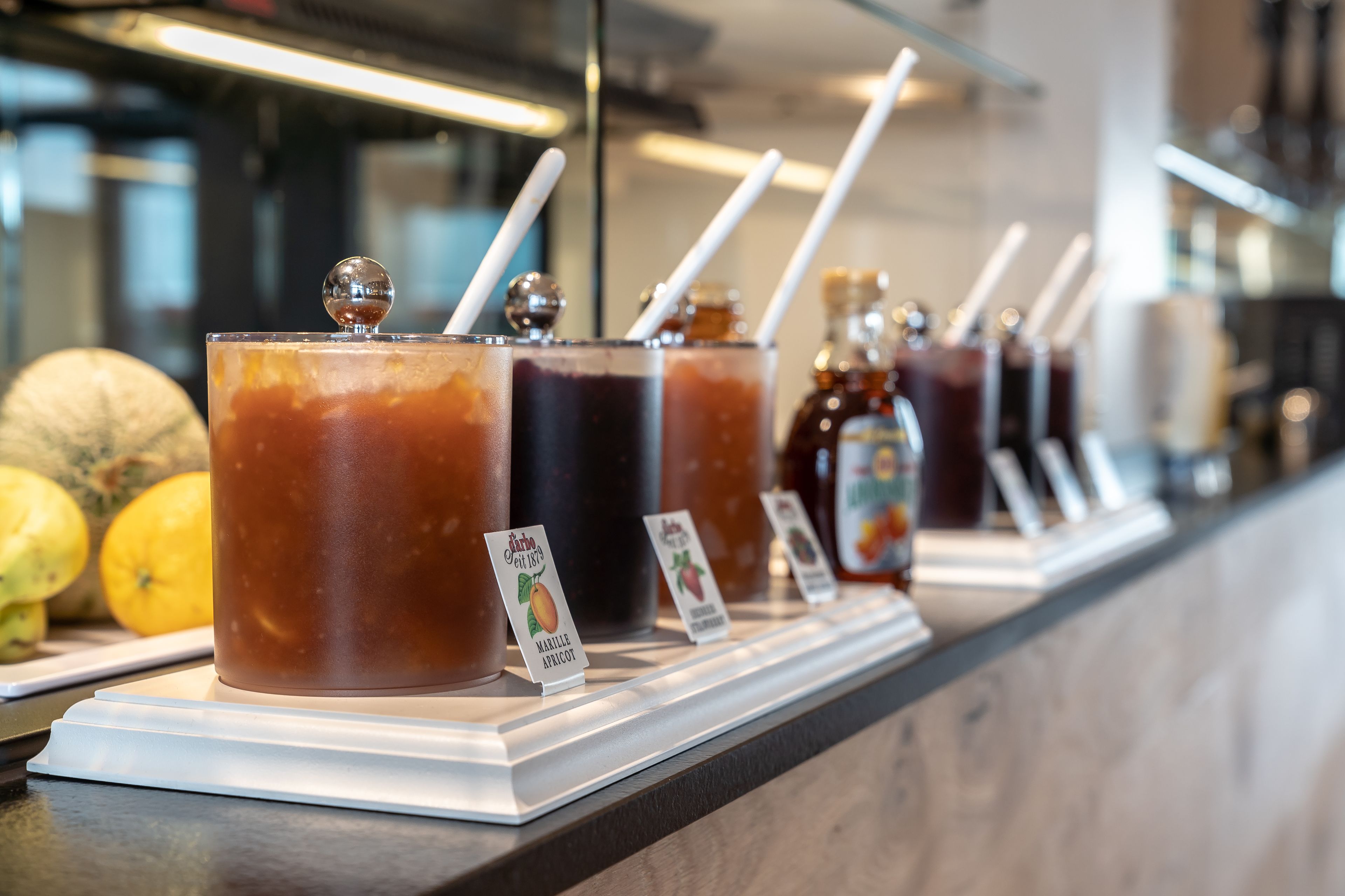 Diversas bebidas geladas com canudos e etiquetas indicando sabores como manga e morango.